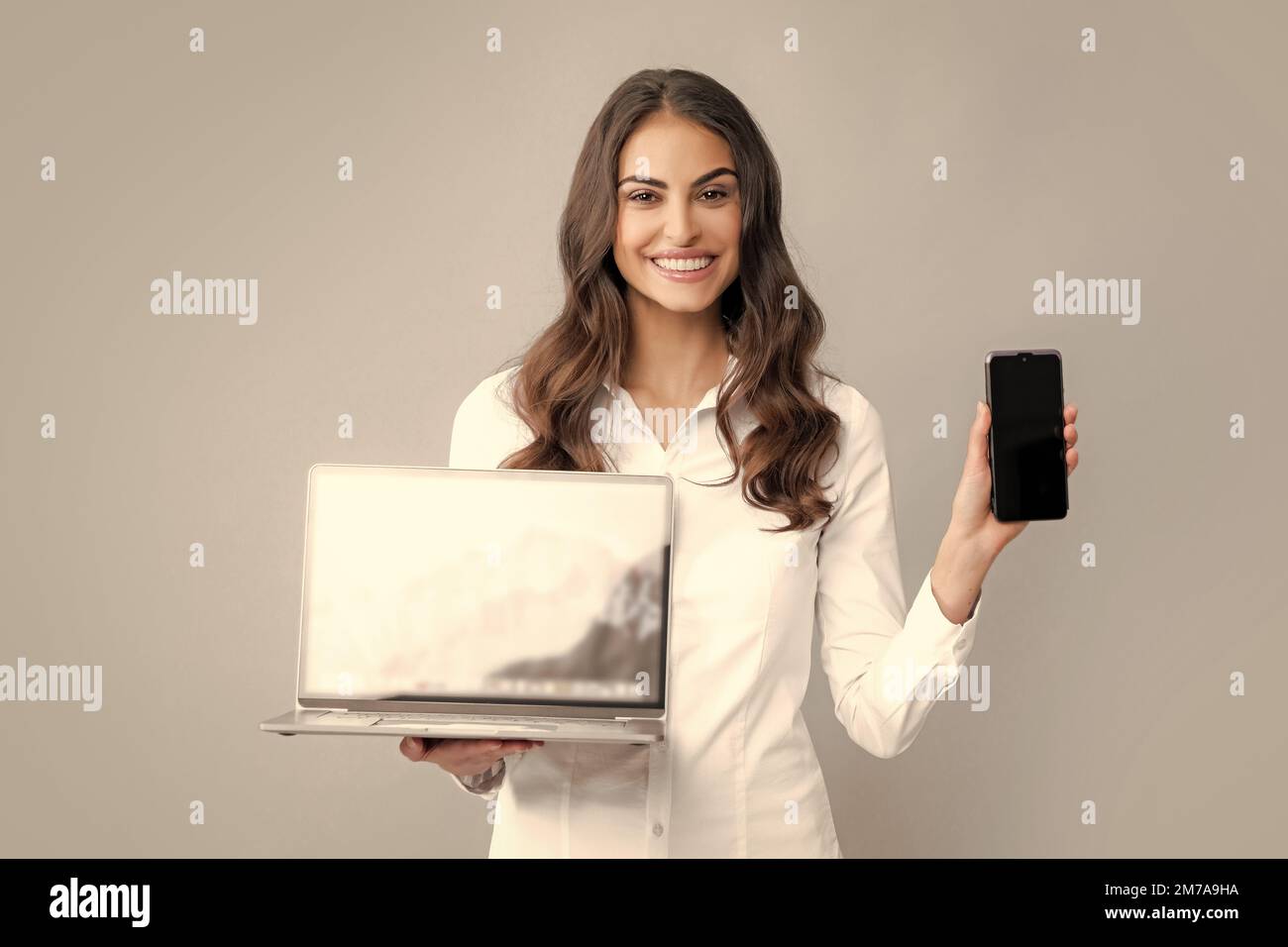 Smiling girl using mobile phone and laptop. Woman showing empty laptop screen, mock up template ...