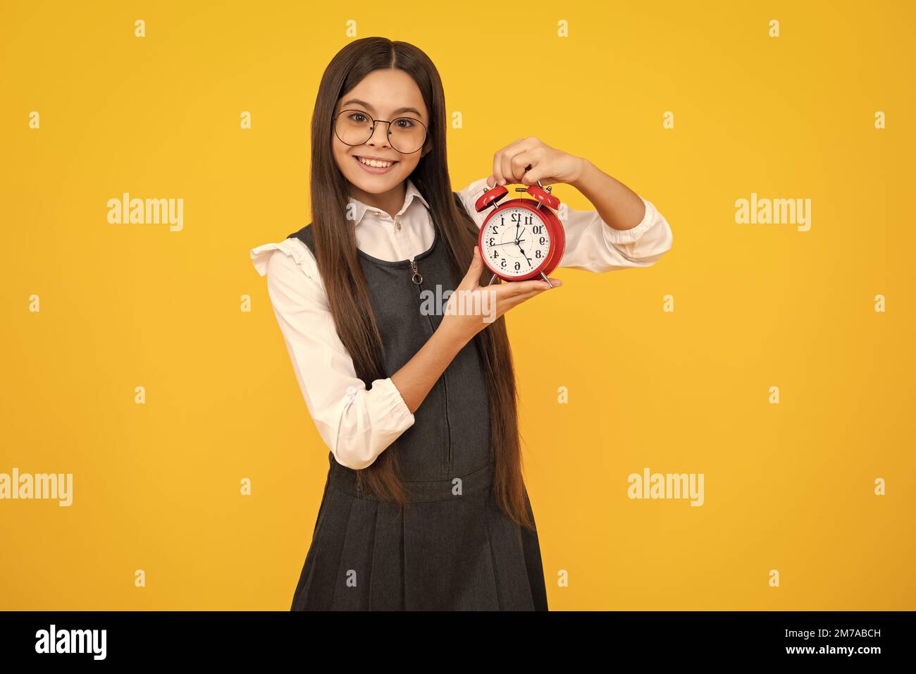 Child student girl with clock isolated on yellow background. Child back ...