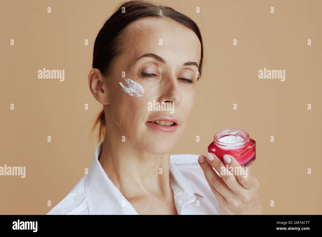 modern woman with facial cream jar in white shirt on beige background ...