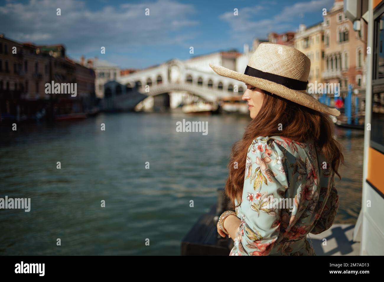 pensive young traveller woman in floral dress with hat on embankment ...