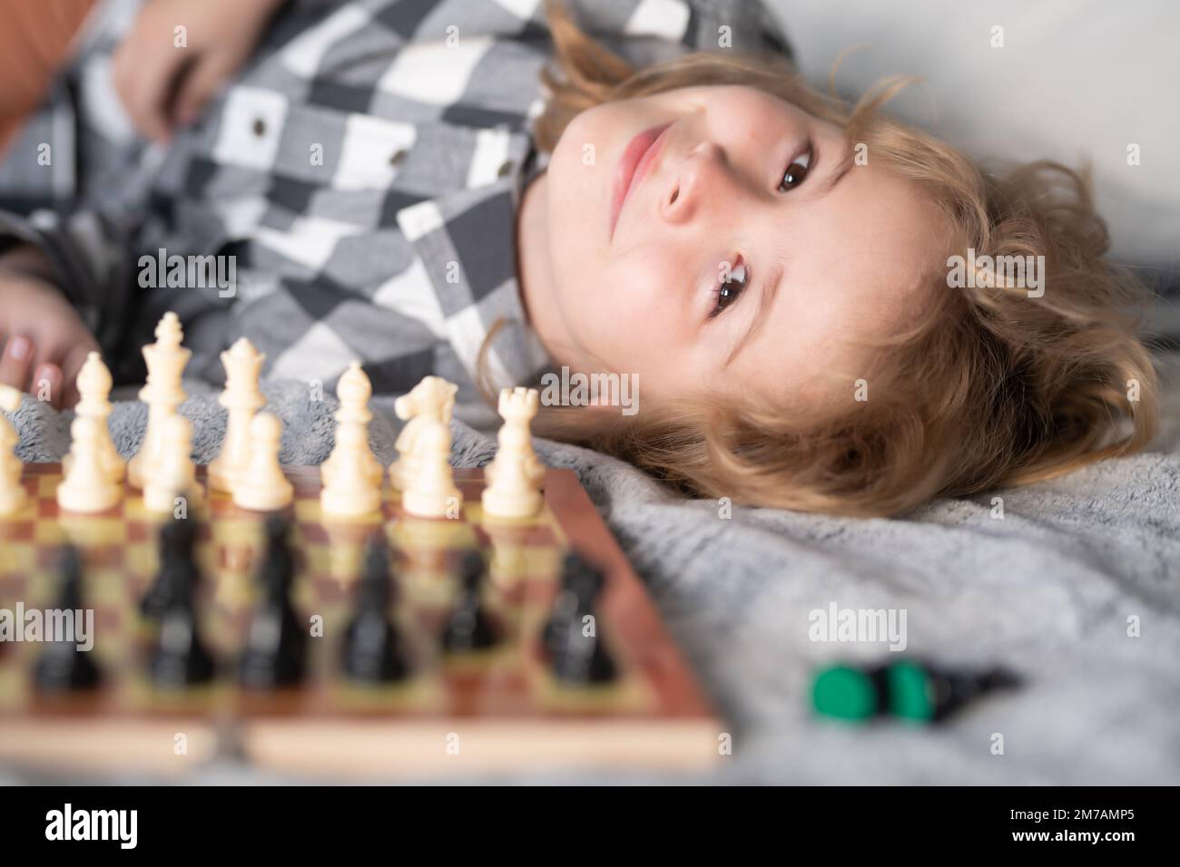 Cute child playing chess on bed at home. Portrait of clever kid with ...