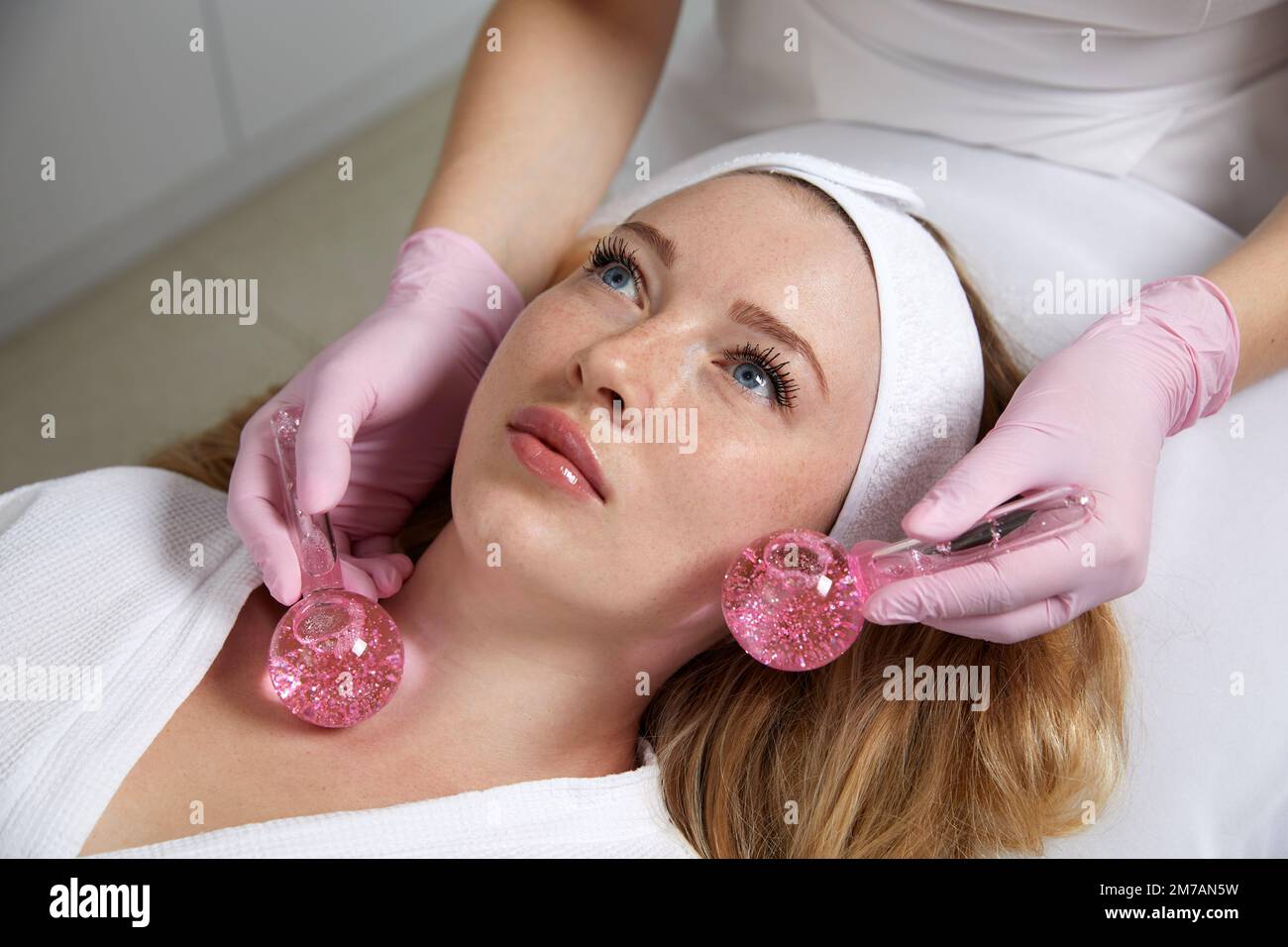 Young woman receiving facial massage with glass balls in beauty salon ...