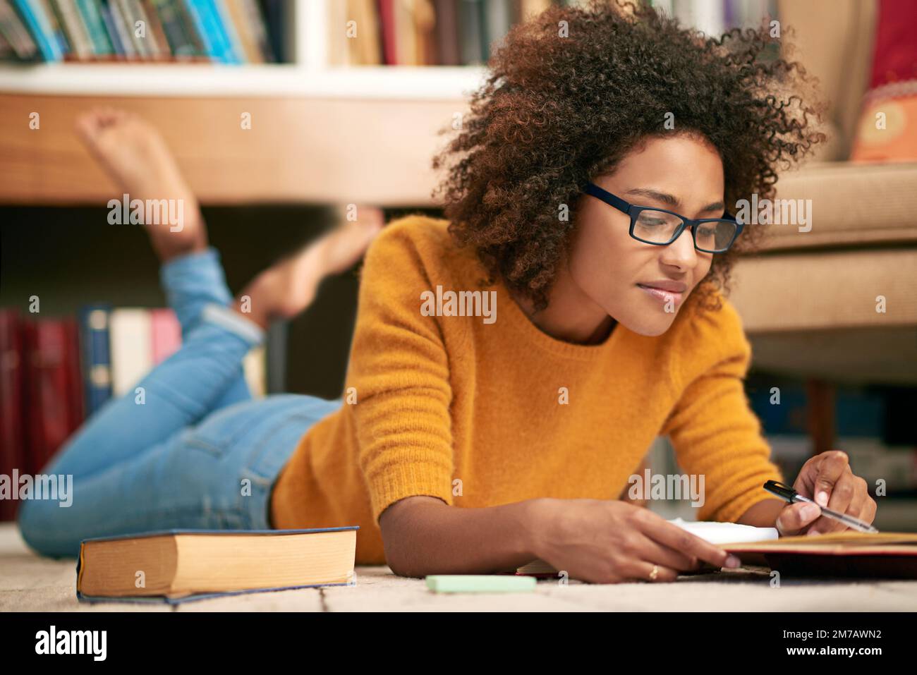 Shes enjoying her required reading. Full length shot of a young woman lying on the floor while ...