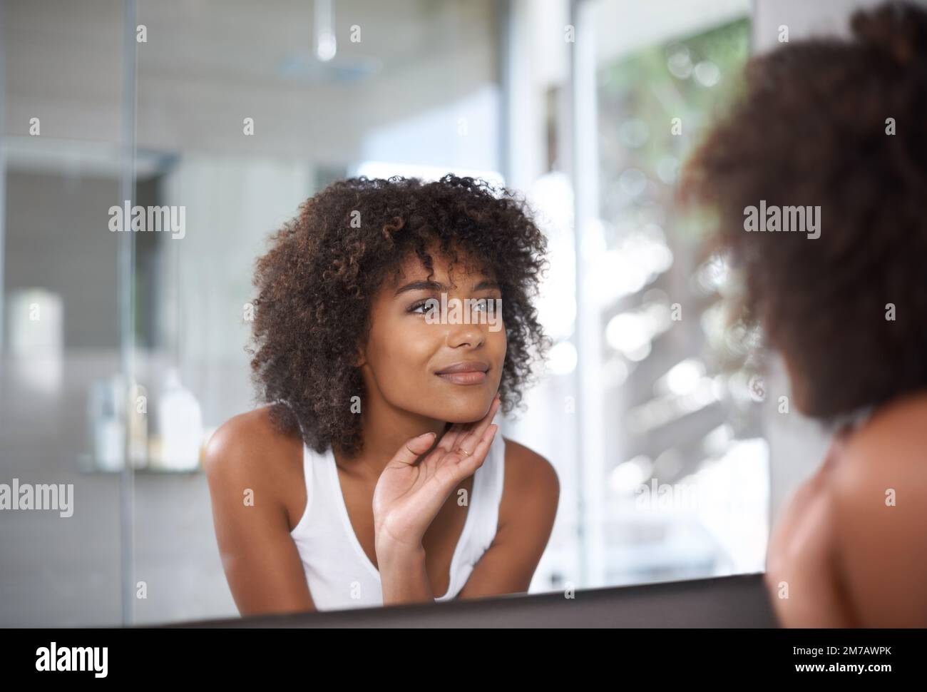 My skin just glows. an attractive young woman looking at herself in the bathroom mirror Stock ...
