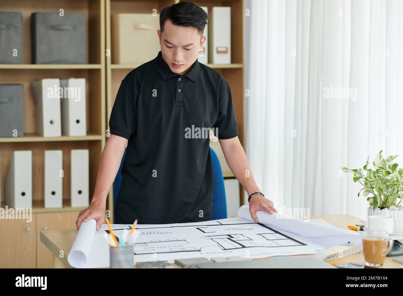 Young architect rolling out house blueprint on table in architecture ...