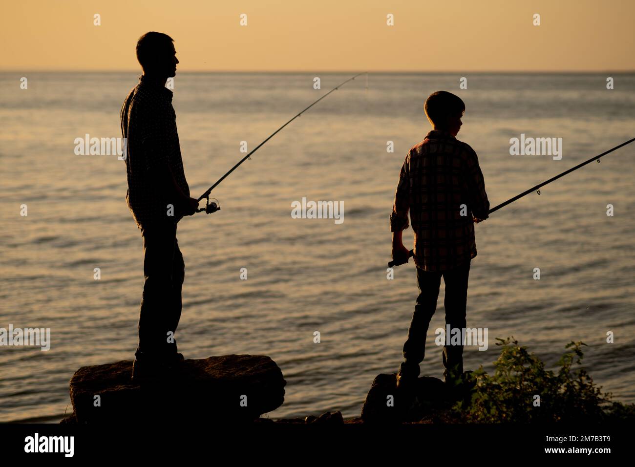 Silhouette of father and son fishing at sunset in summer on the sea ...