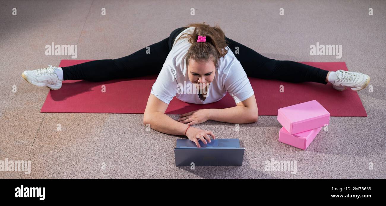 Young caucasian fat woman doing bends on a sports mat and watching a ...