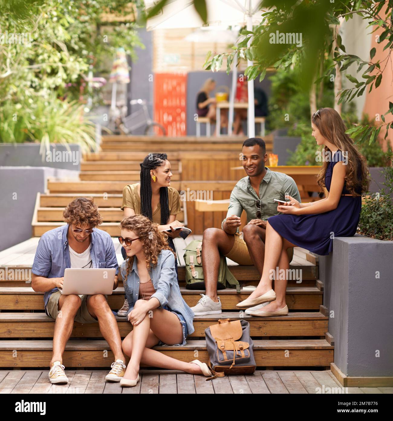 Chilling on campus between classes. A group of young friends using their laptops and cellphones ...