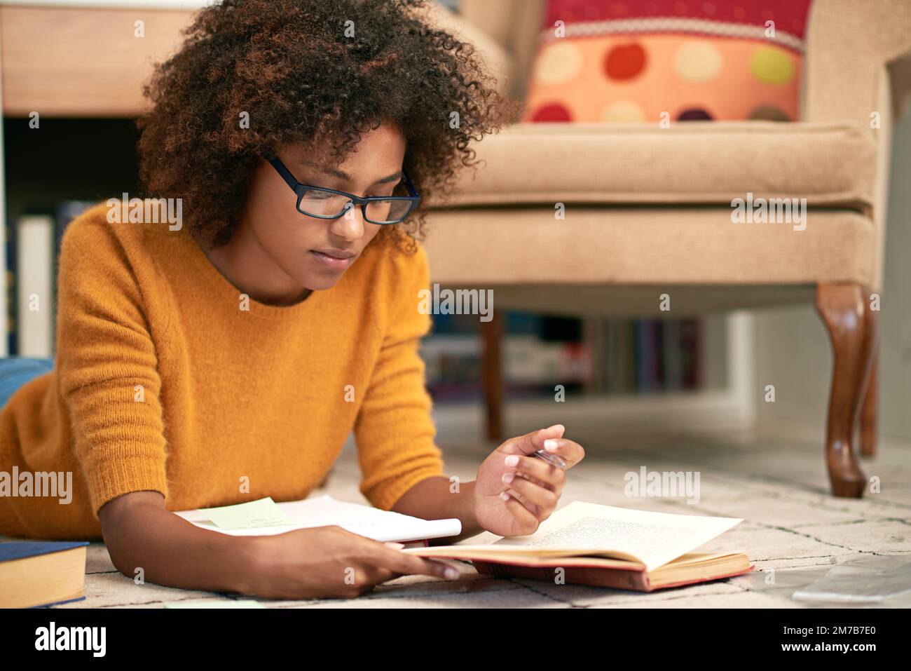 Focused on her studies. a young woman lying on the floor while studying ...