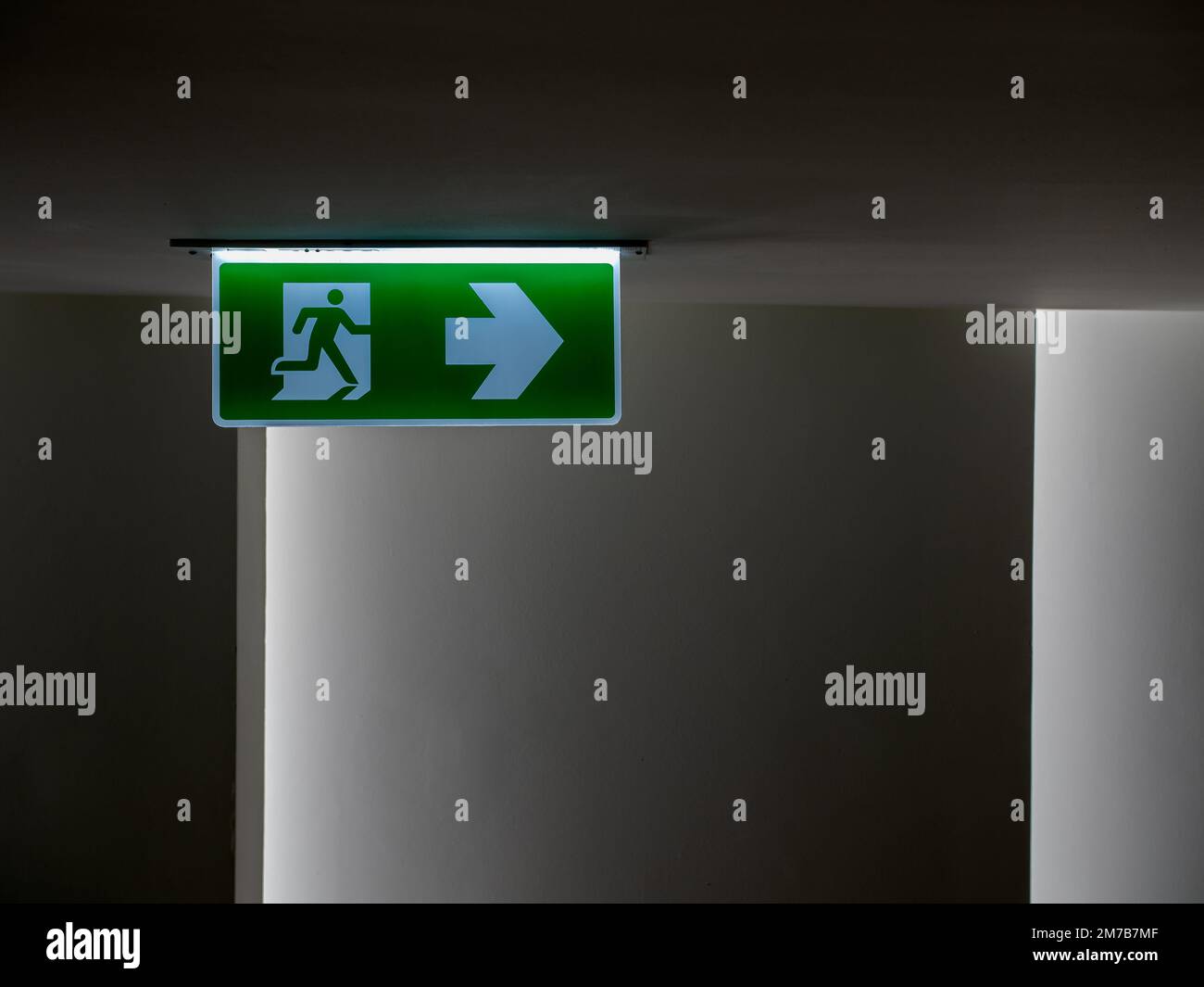Green fire escape sign hang on the ceiling in the dark building ...