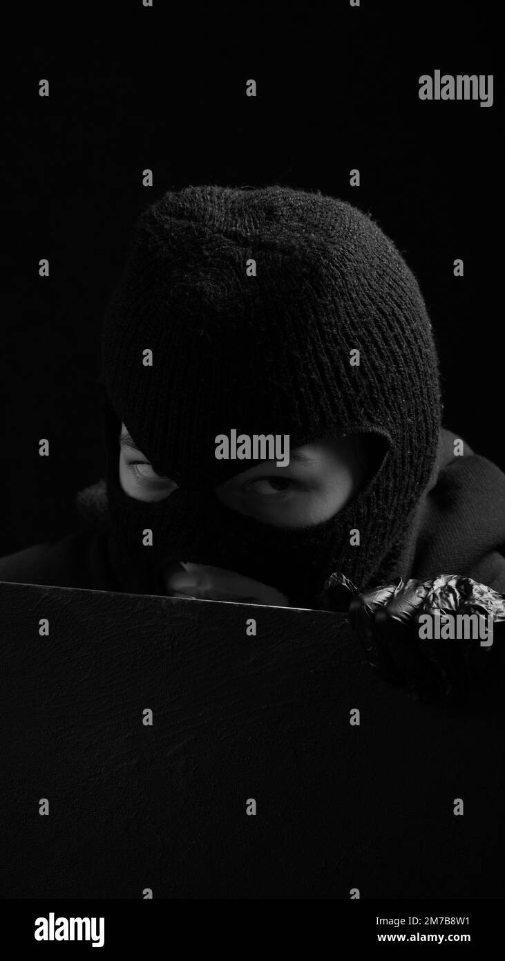 Masked female burglar in black gloves looks over a fence. Crime concept ...