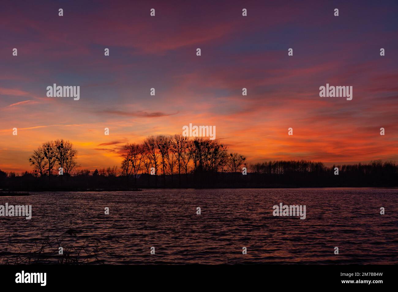Beautiful colorful clouds after sunset over trees and lake water ...