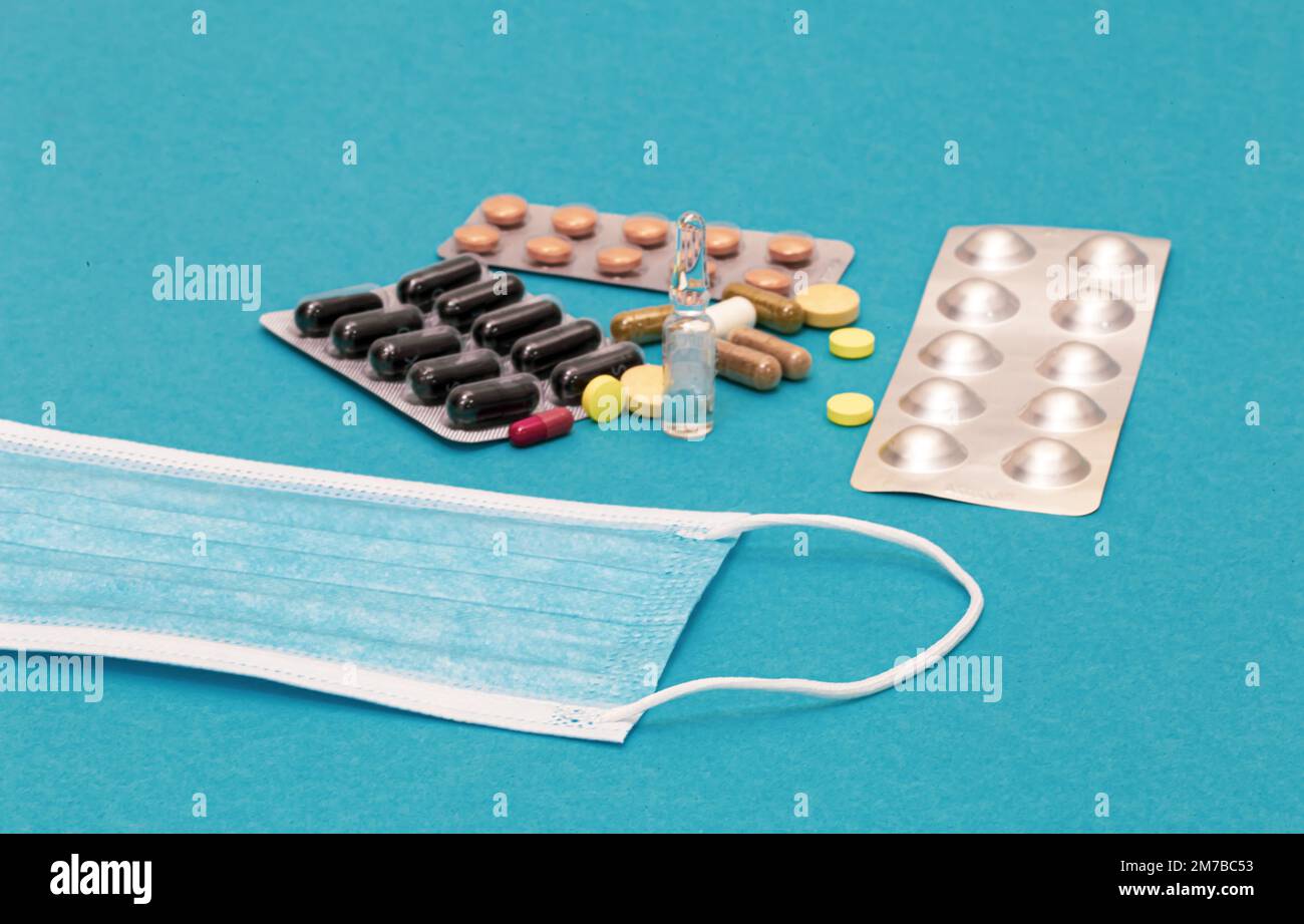 A variety of pills and a protective face mask on a blue background ...