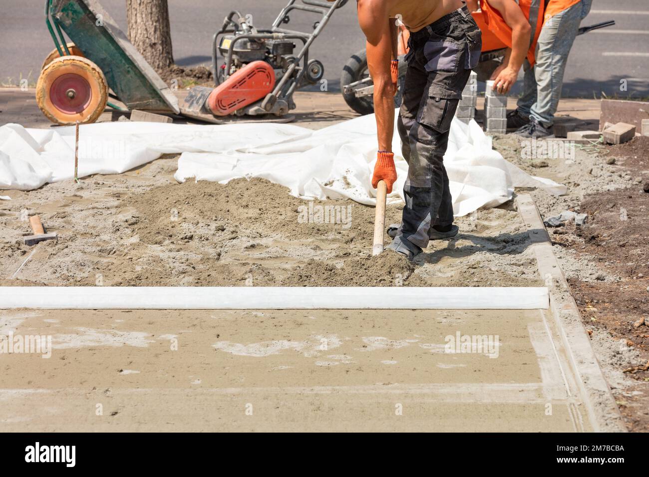 A team of workers with a shovel levels the sand base at the workplace ...