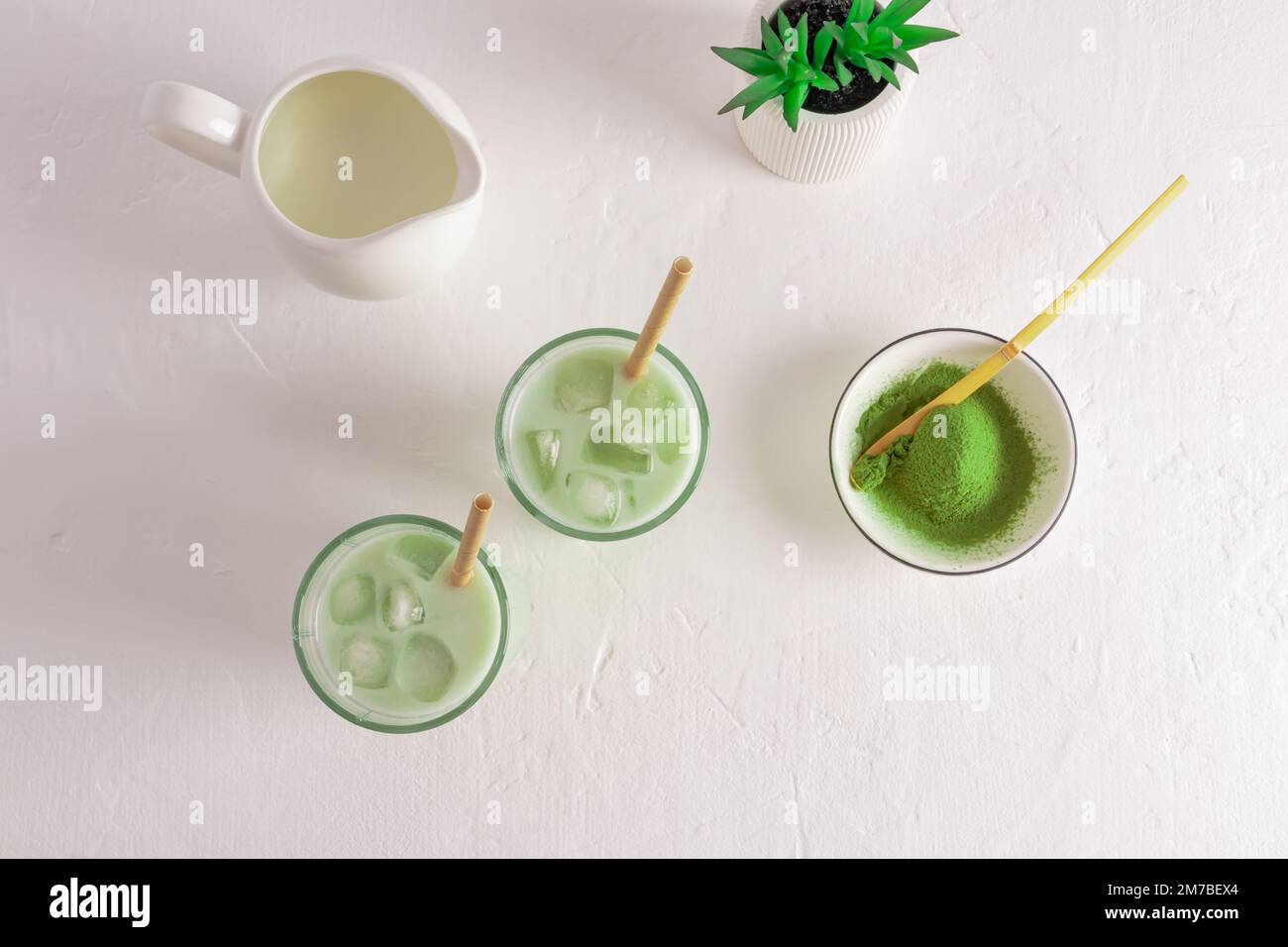 two glasses with green iced tea matcha latte, a bowl of matcha powder ...