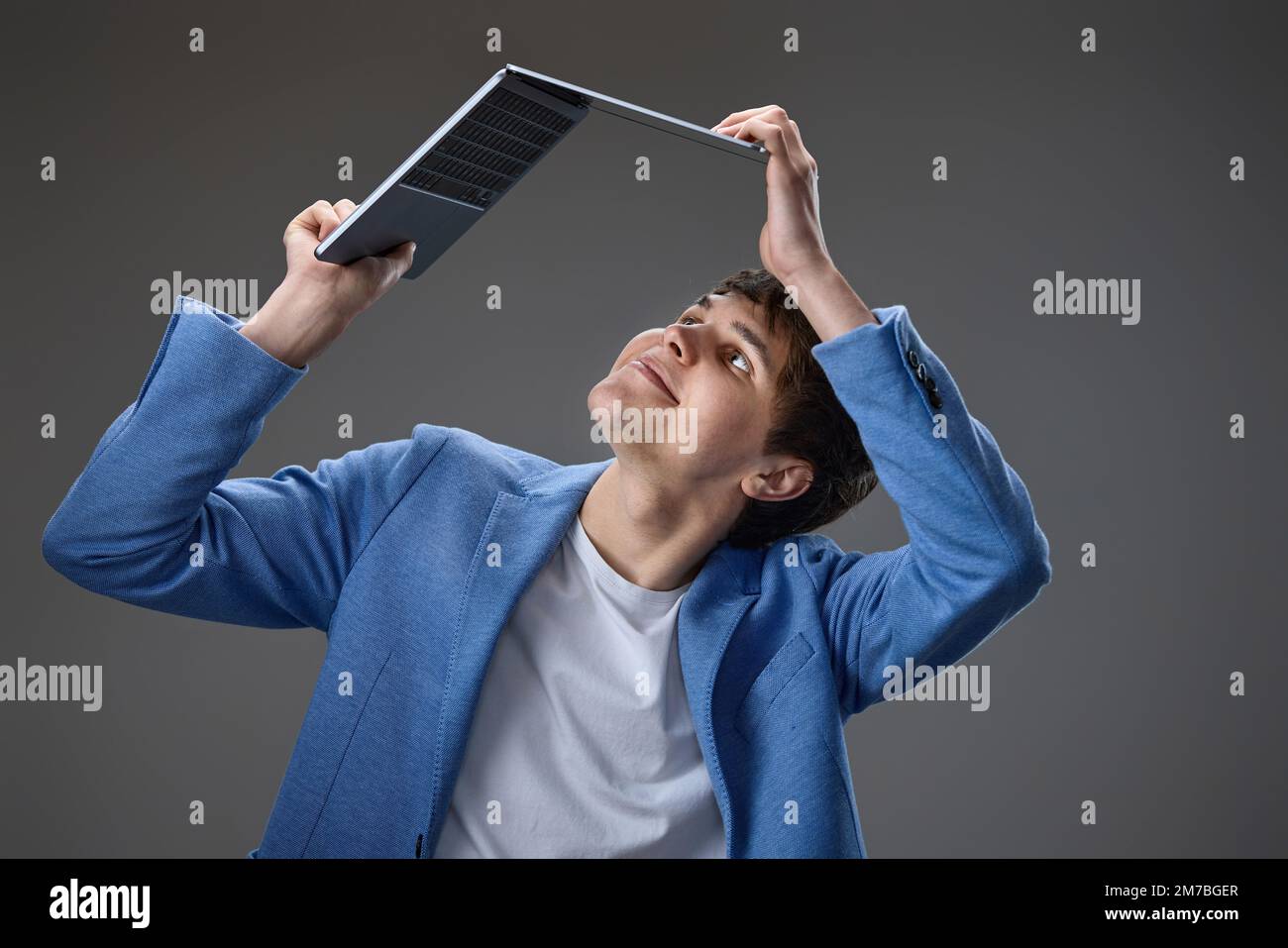 happy caucasian young guy in blue jacket holding laptop computer over ...