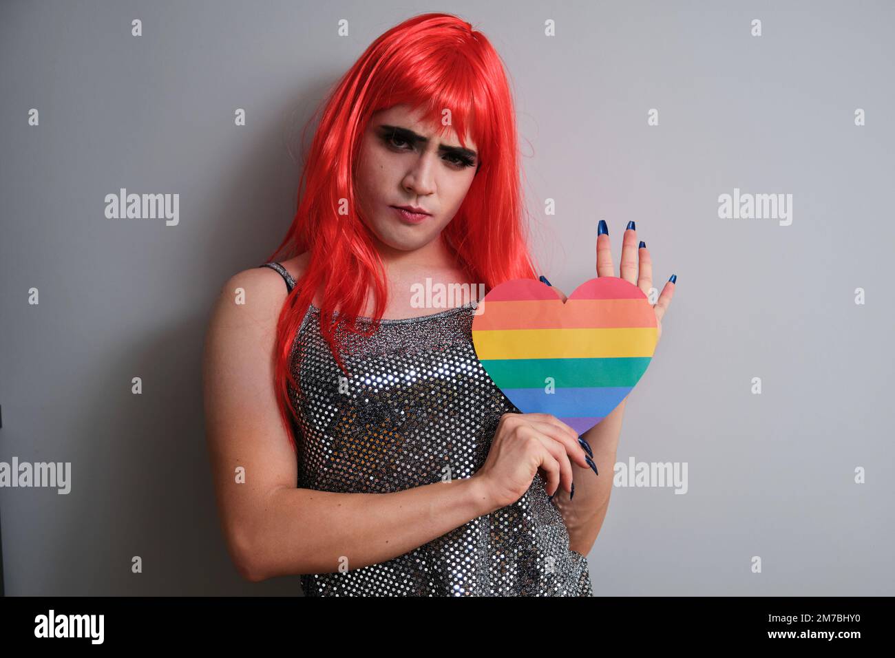 Portrait of transgender man holding a rainbow flag heart on grey ...