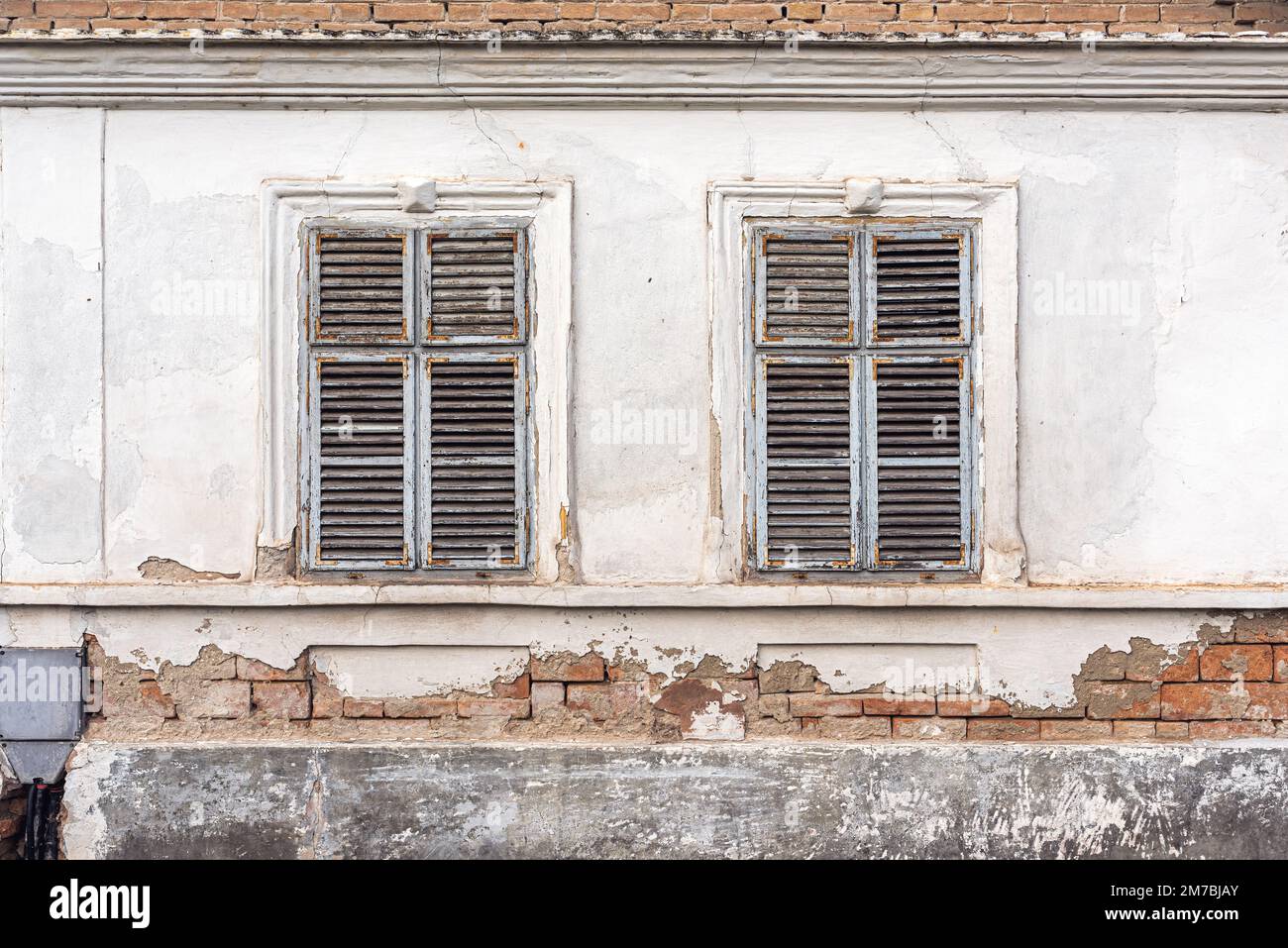 Old ruined house building facade with worn wooden windows with shutters ...