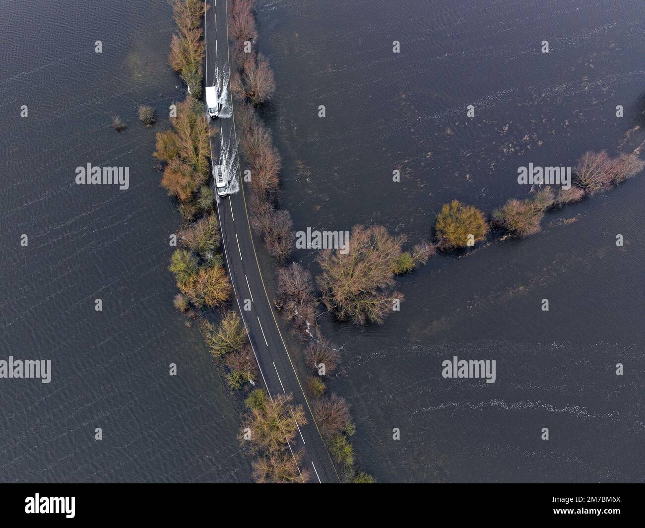 Vehicles travel along the road as the Welney wash fills with floodwater ...