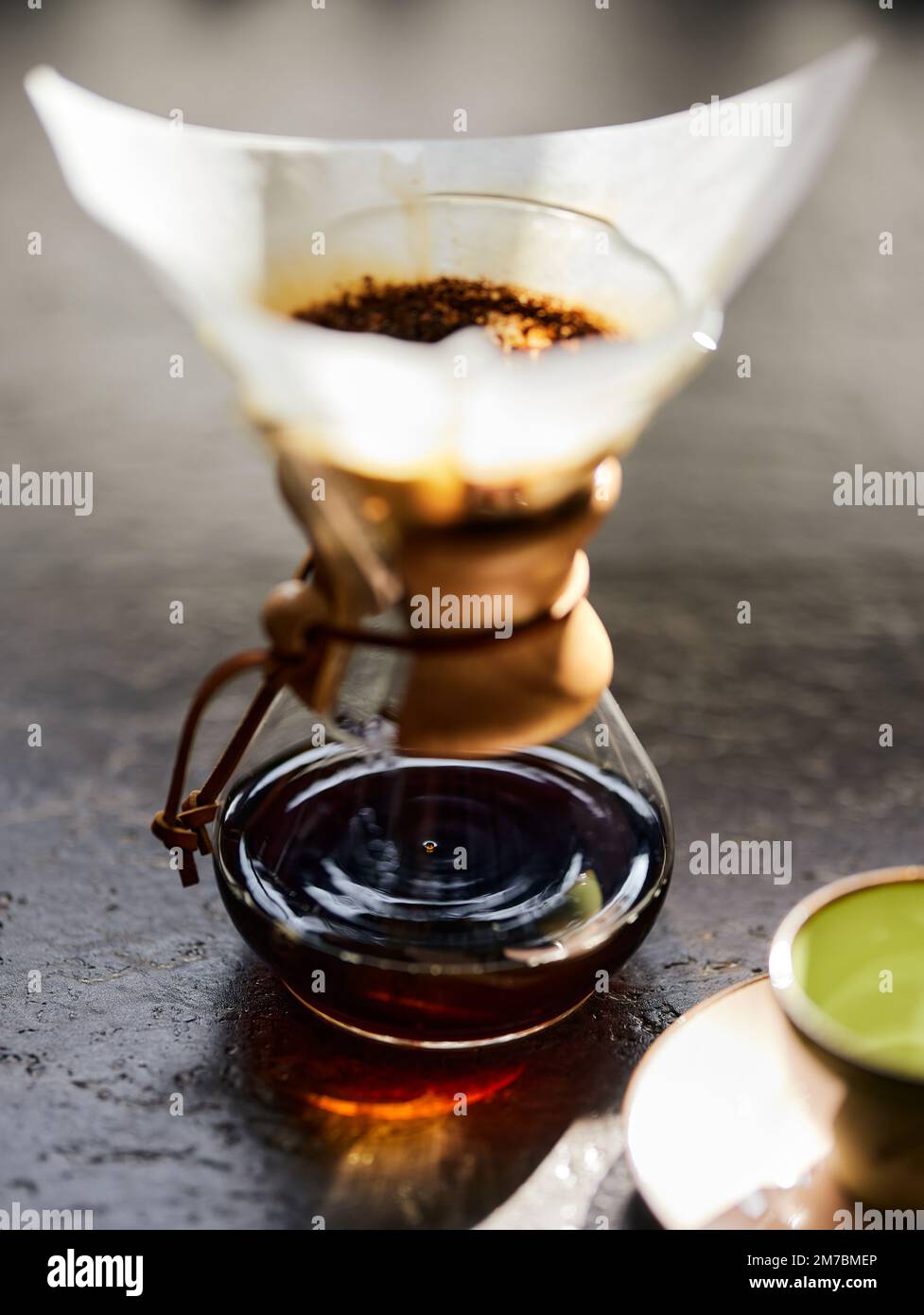 A vertical closeup shot of coffee dripping through a paper filter over ...