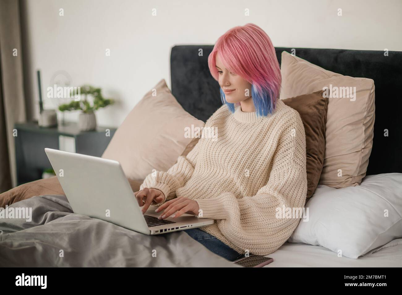 Concentrated pink-haired girl typing on the laptop in the bedroom Stock ...