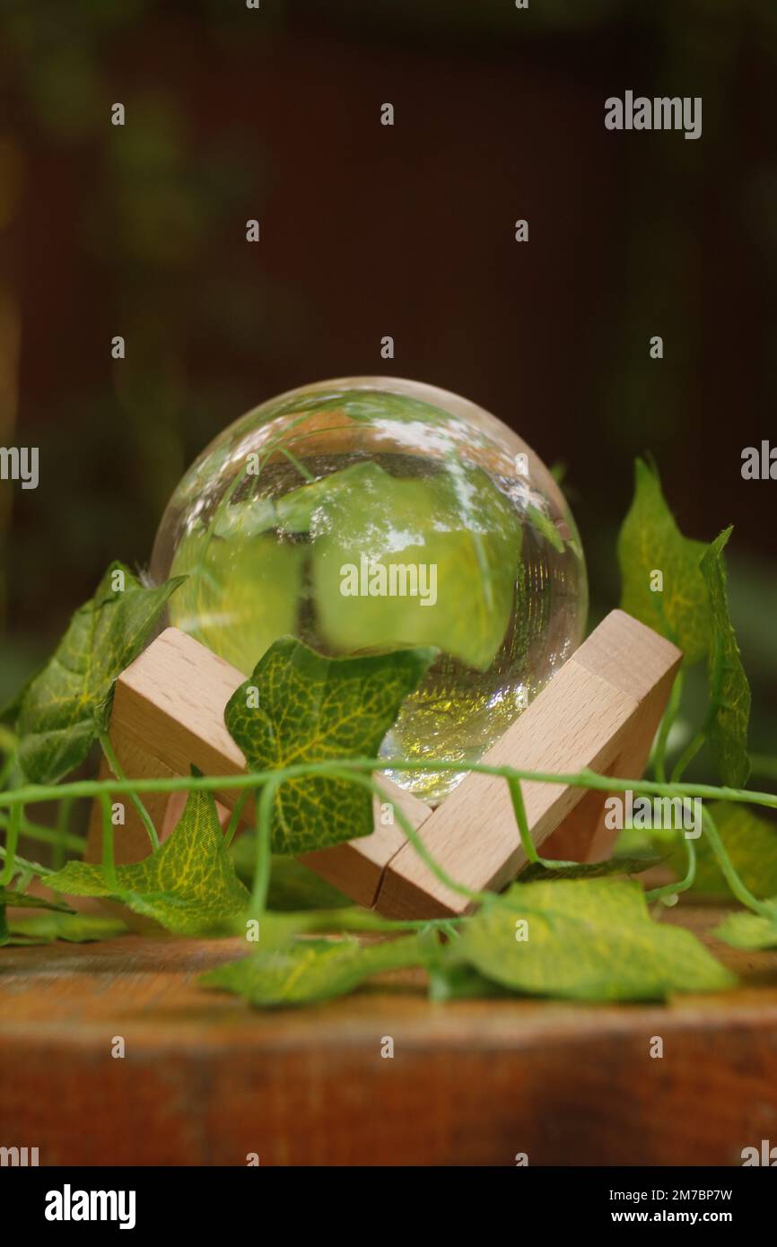 A vertical shot of a glass ball in a wooden frame surrounded by leaves ...