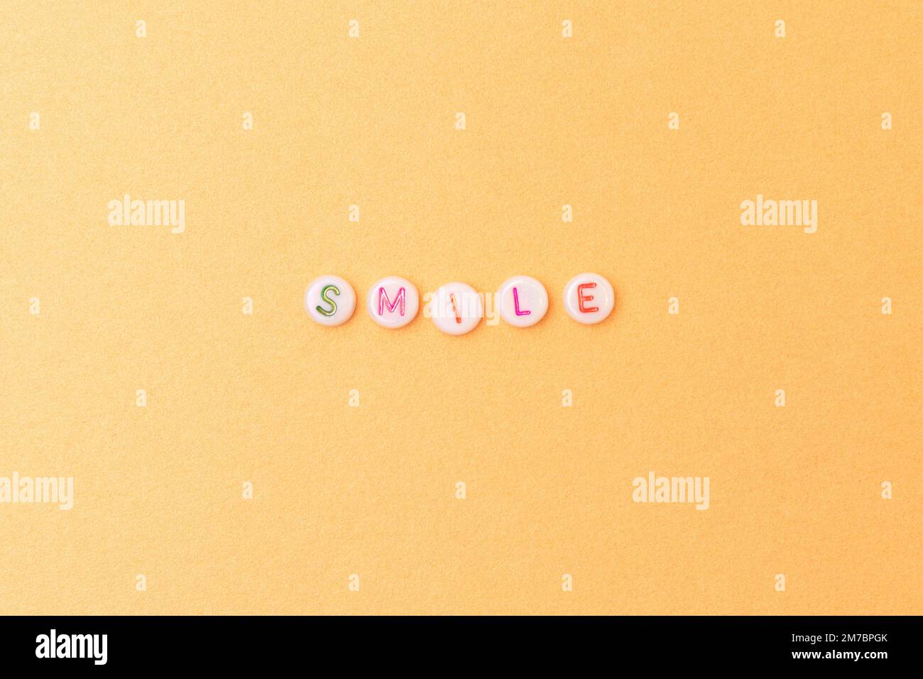 Word Smile. Quote made of white round beads with multicolored letters ...