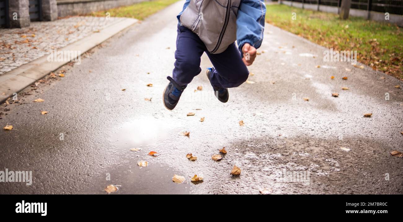 A child jumps over a puddle of water and leaves - the road in the ...