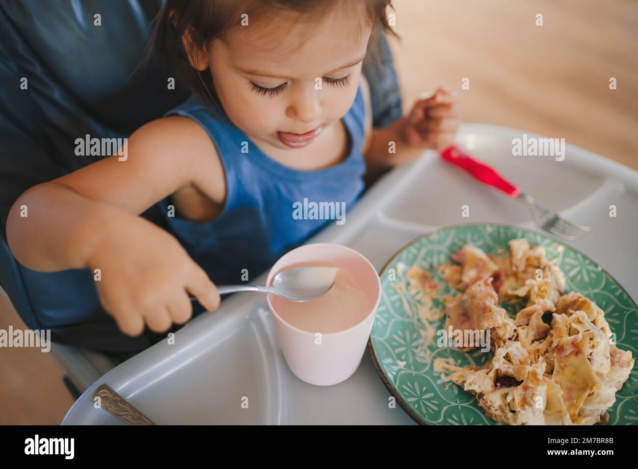 Cute baby girl eating food by herself, sitting on high chair. Caucasian ...