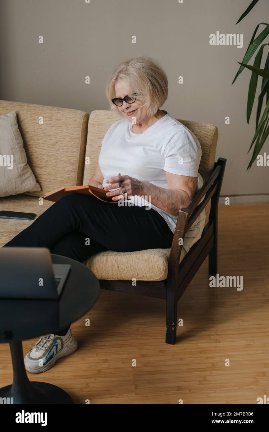 Positive senior woman wearing eyeglasses working remotely while sitting ... Positive senior woman wearing eyeglasses working remotely while sitting ...