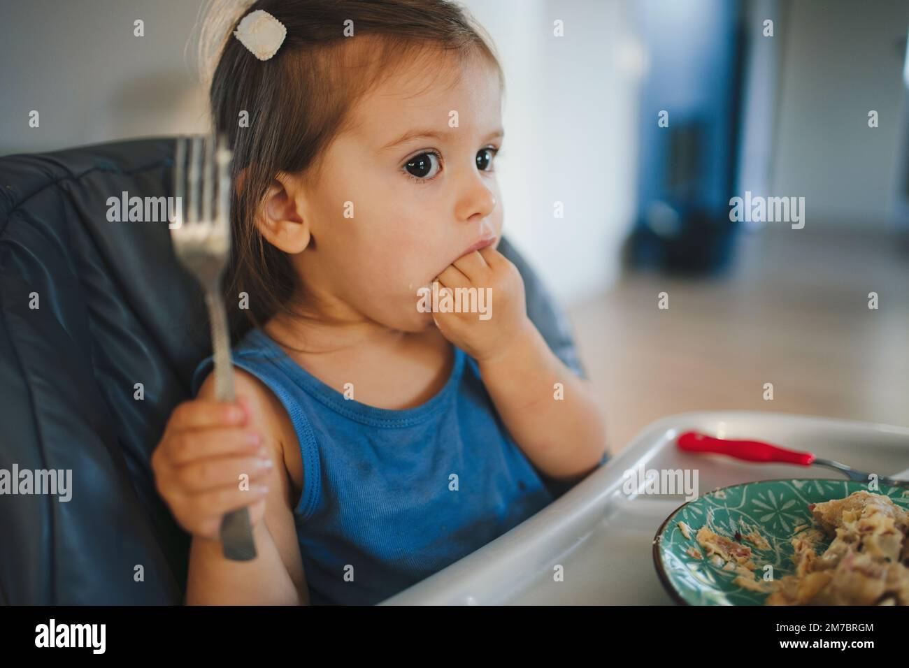 Hungry baby girl eating with pleasure her meal by hand, sitting in high ...