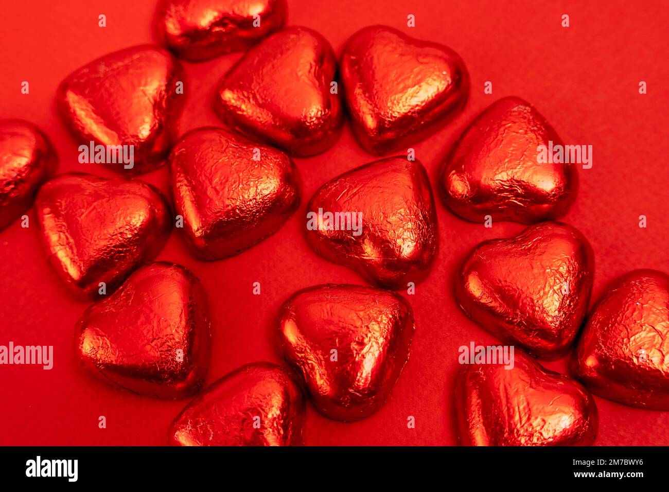 lots of heart-shaped candies wrapped in red foil on a red background ...