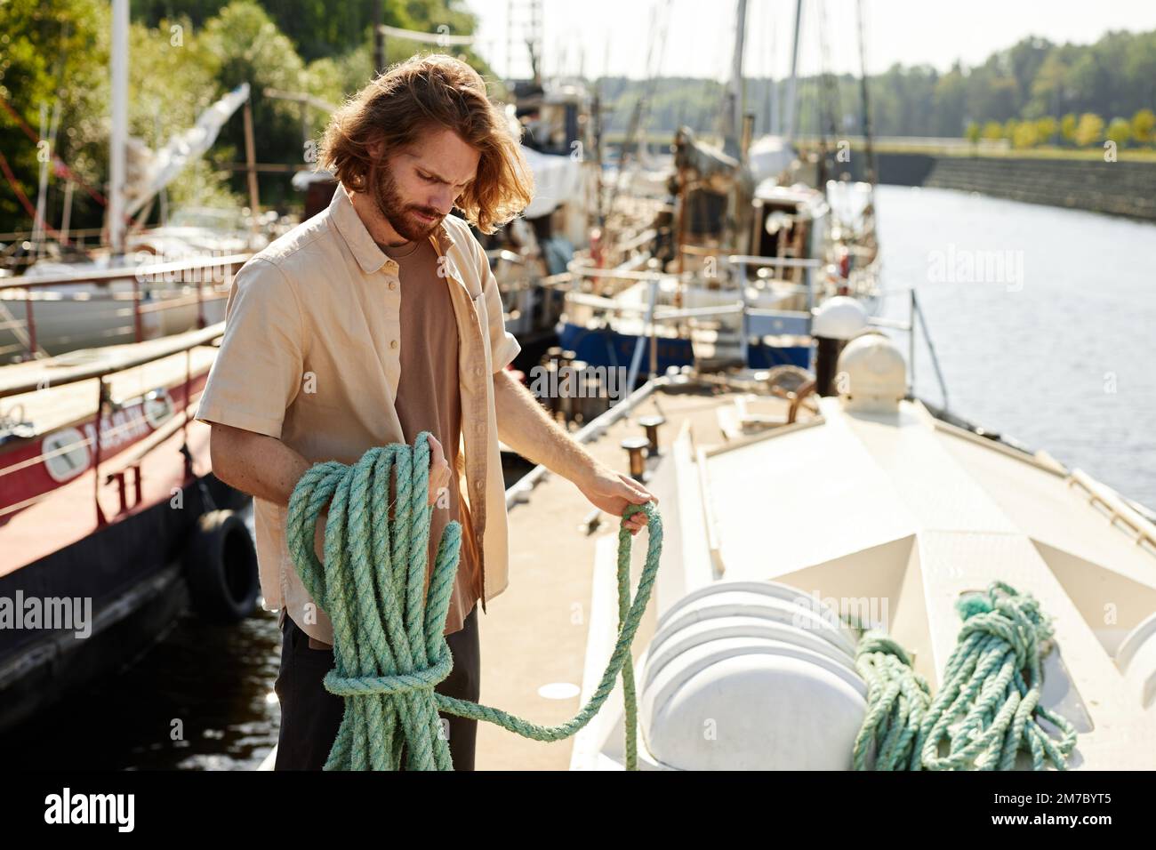 Portrait of handsome long haired man standing on boat in dock and ...