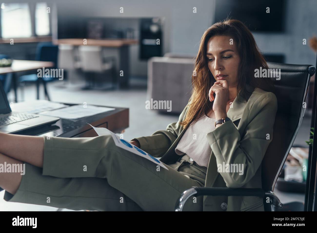 Woman reading document sitting in office with her legs on desk Stock ...