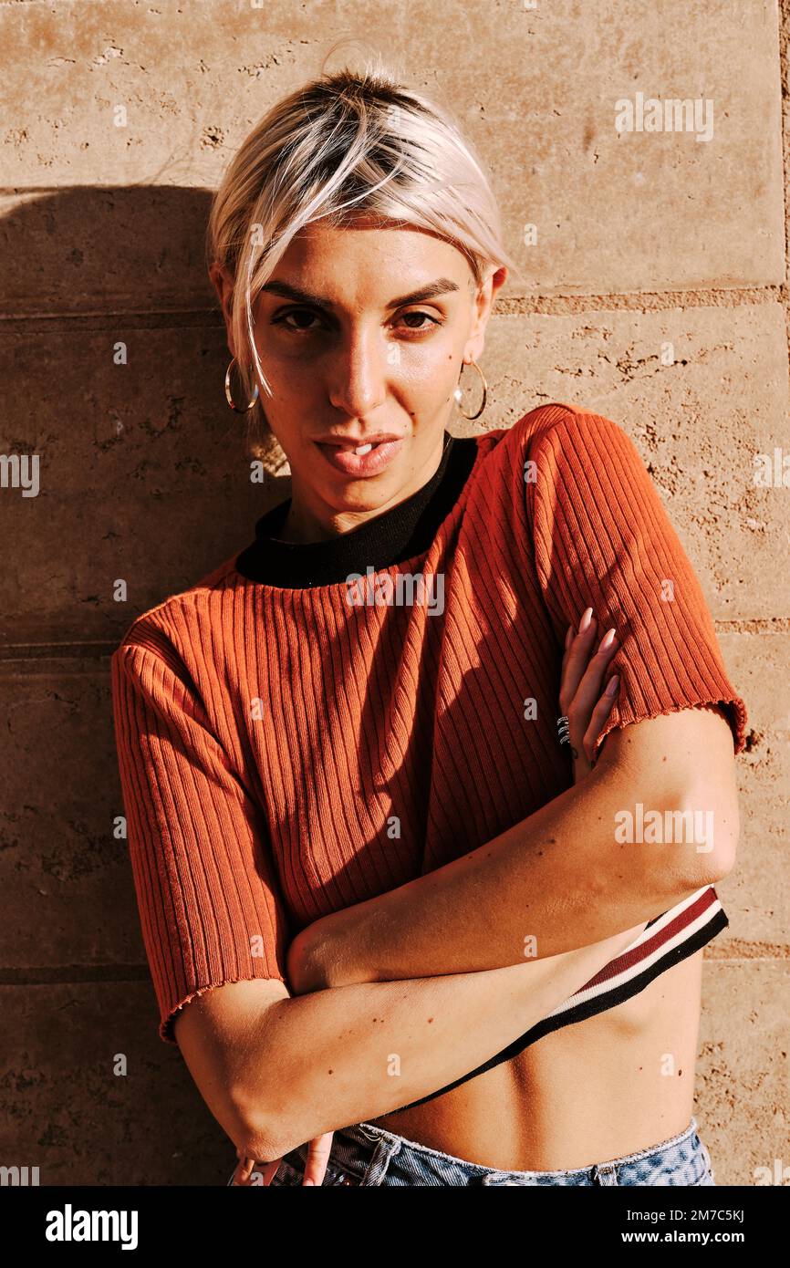 Woman with a serious face posing with her arms crossed against a wall ...