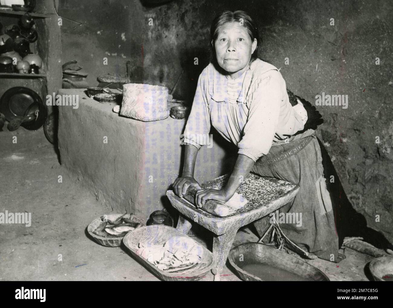 Tarascan woman grinding corn on the metate quern in a village, Ihuatzio ...