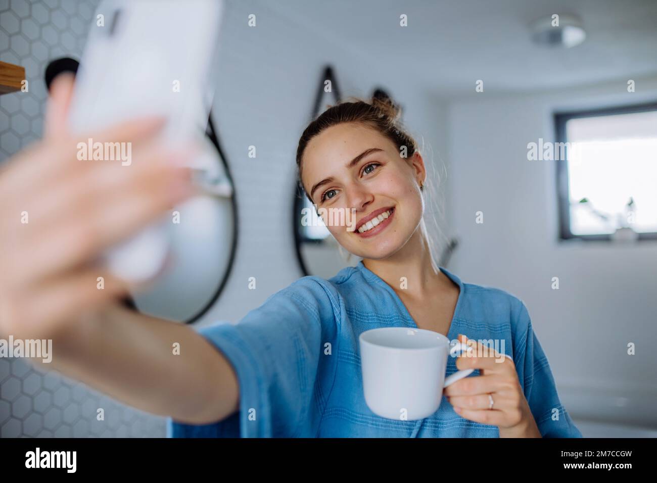 Young woman taking selfie in bathroom, enjoying cup of coffee Stock ...