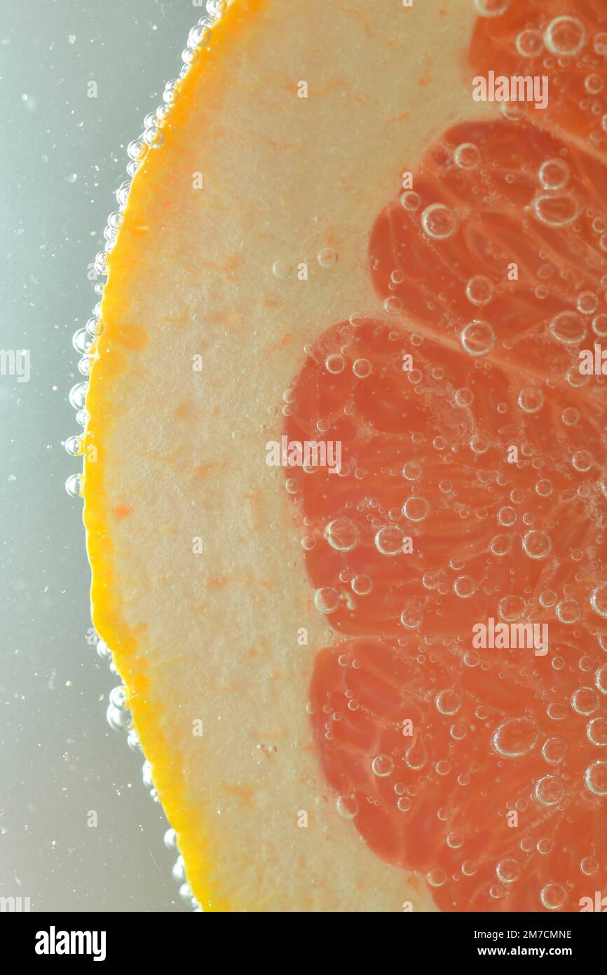 Close-up of fresh grapefruit slice on white background. Slice of red grapefruit in sparkling ...