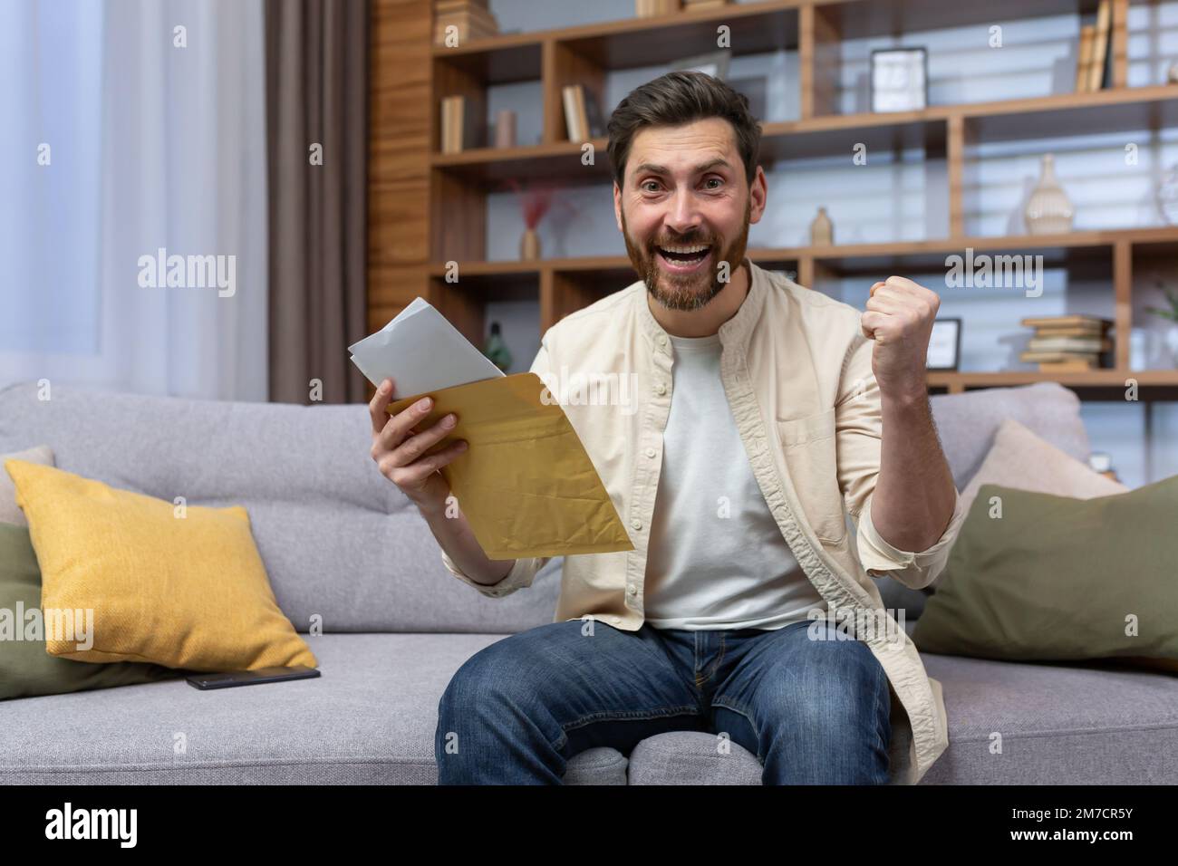 Portrait of happy man at home sitting on sofa rejoicing and celebrating ...