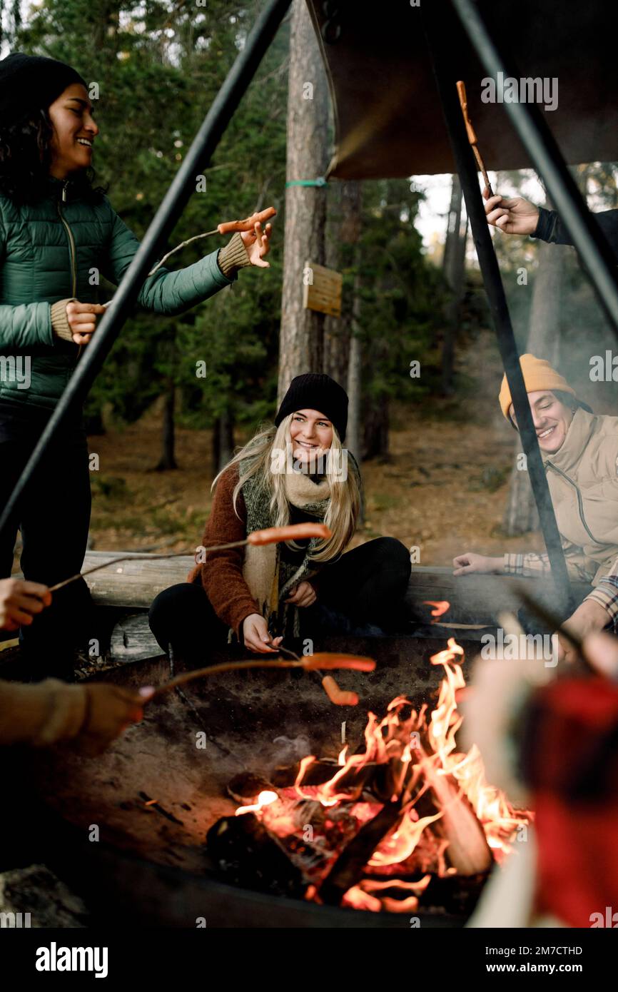 Happy male and friends enjoying food at campfire in forest Stock Photo ...