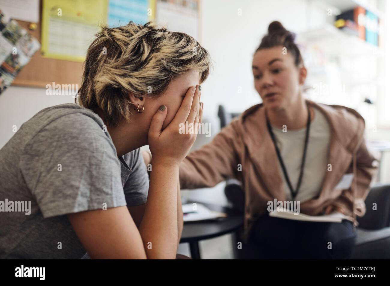 Non-binary counselor consoling female student covering face with hand ...