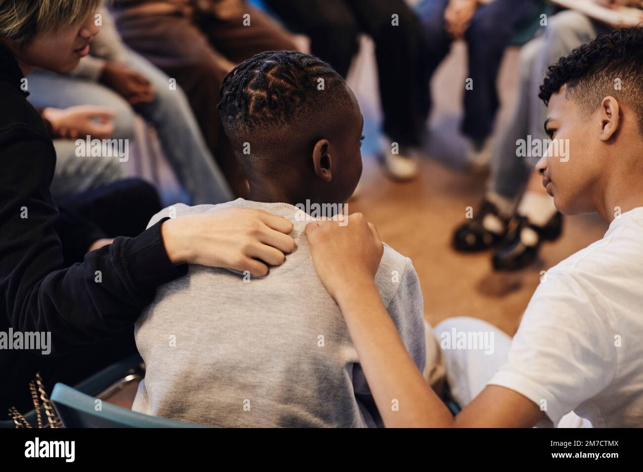 Multiracial boys consoling male friend with arms around in group ...