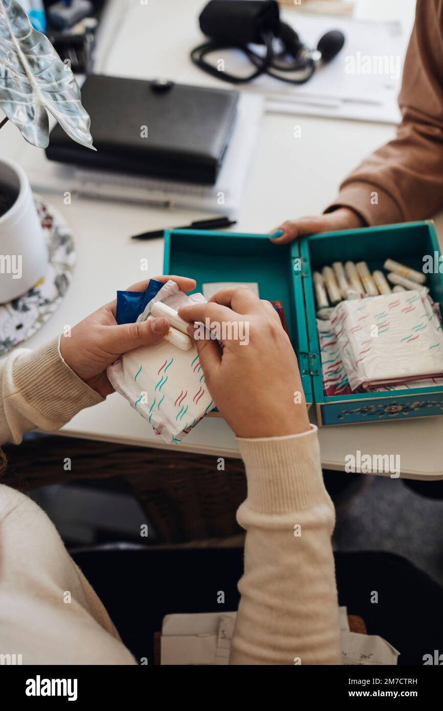 Hands of female student holding sanitary pads and tampons at table in ...