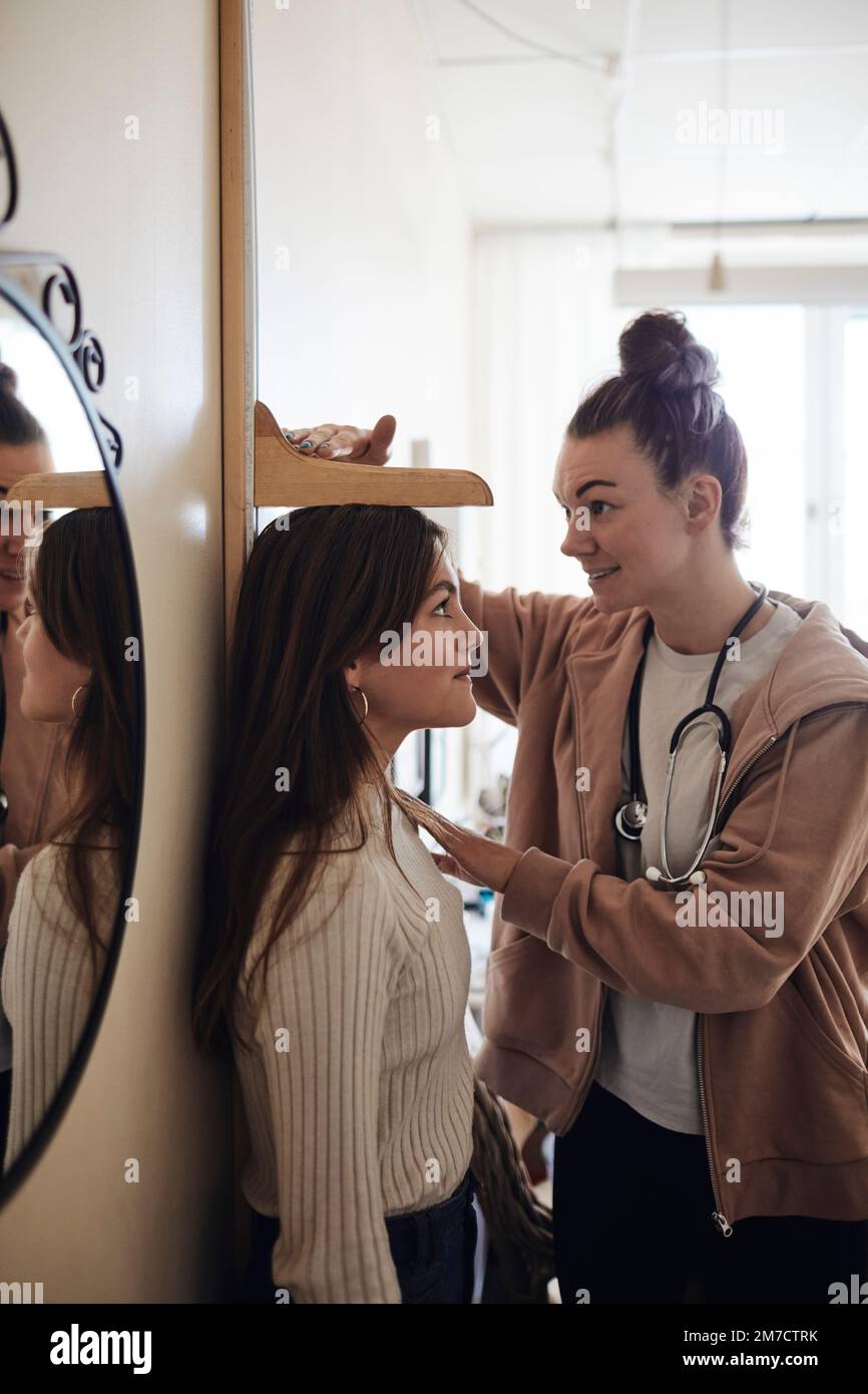 Smiling school nurse measuring height of female student standing by ...