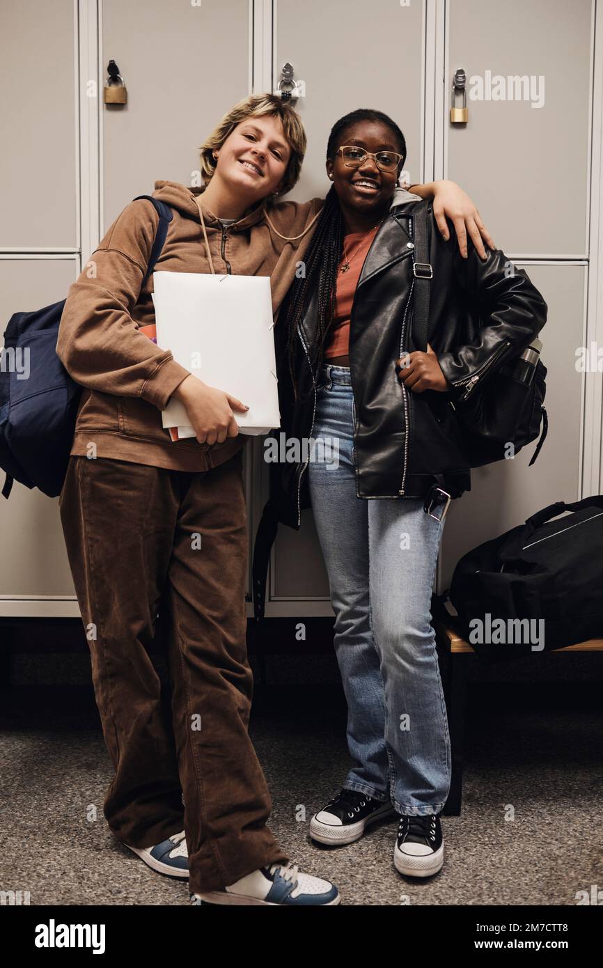 Full length portrait of smiling teenage girl standing with arm around ...