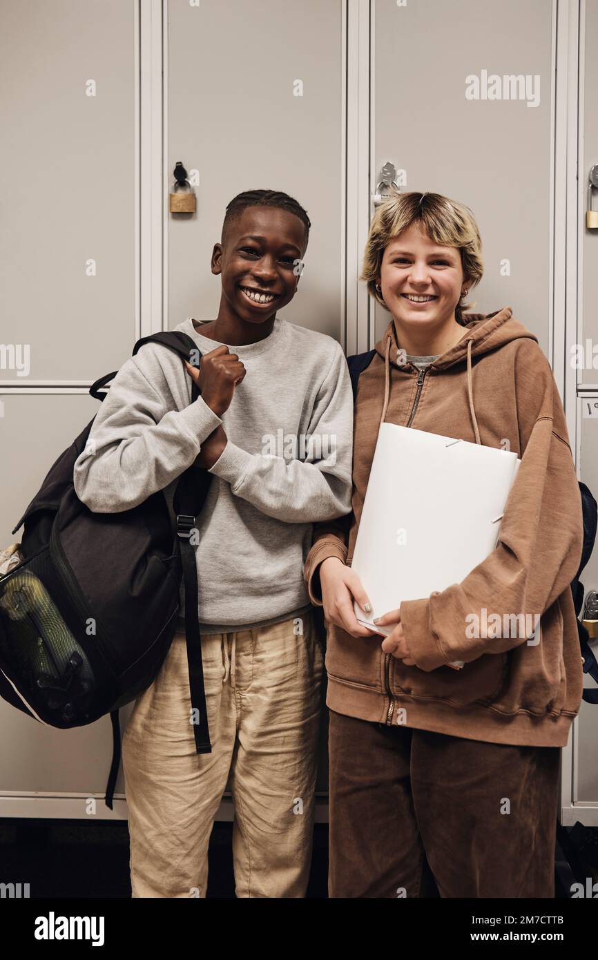 Portrait of happy teenage boy and girl standing against locker in ...