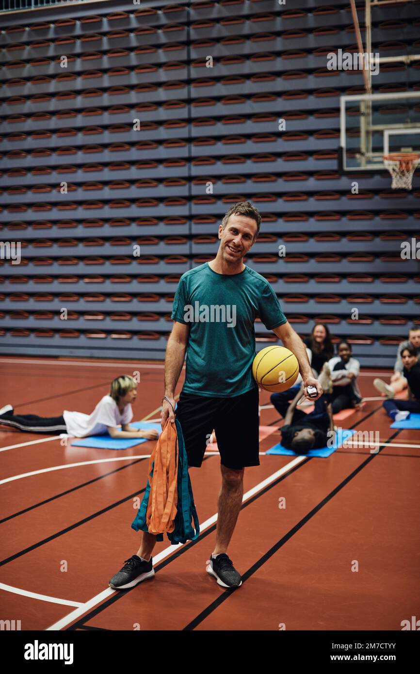 Full length portrait of smiling male coach standing with basketball ...