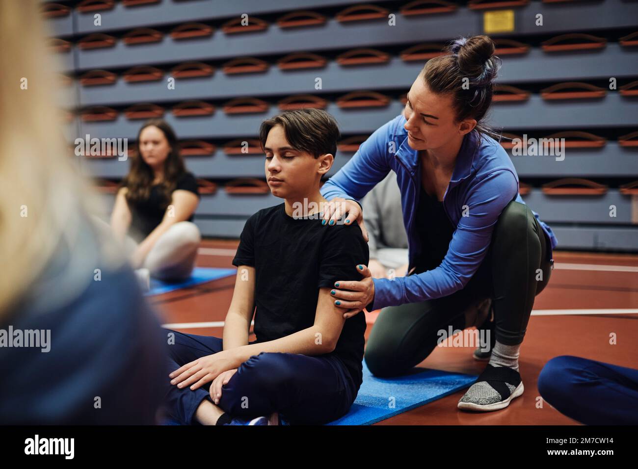 Female coach guiding male student sitting with eyes closed in sports ...