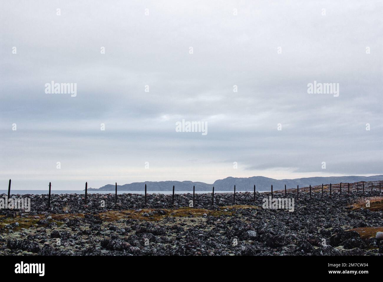 A landscape of rocky coast with wooden poles by Kola river under gray ...