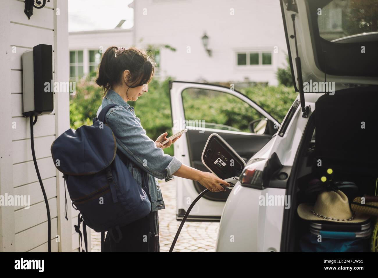 Side view of woman using smart phone while charging electric car Stock ...